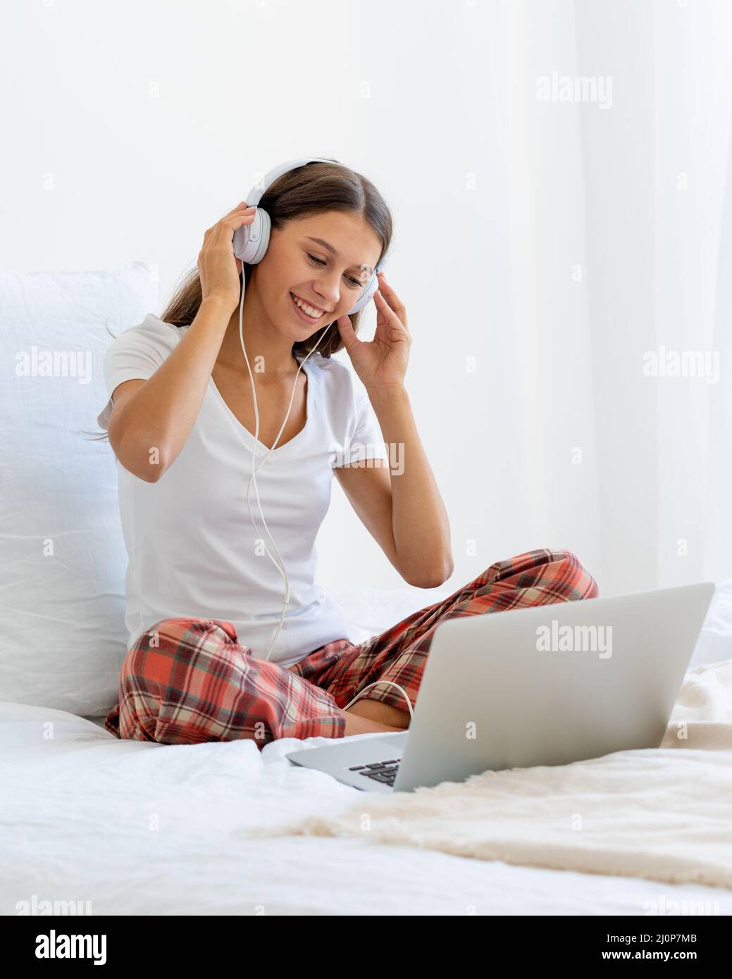 Young Smiling Woman Sitting On Bed In Bedroom And Listening To Music Or