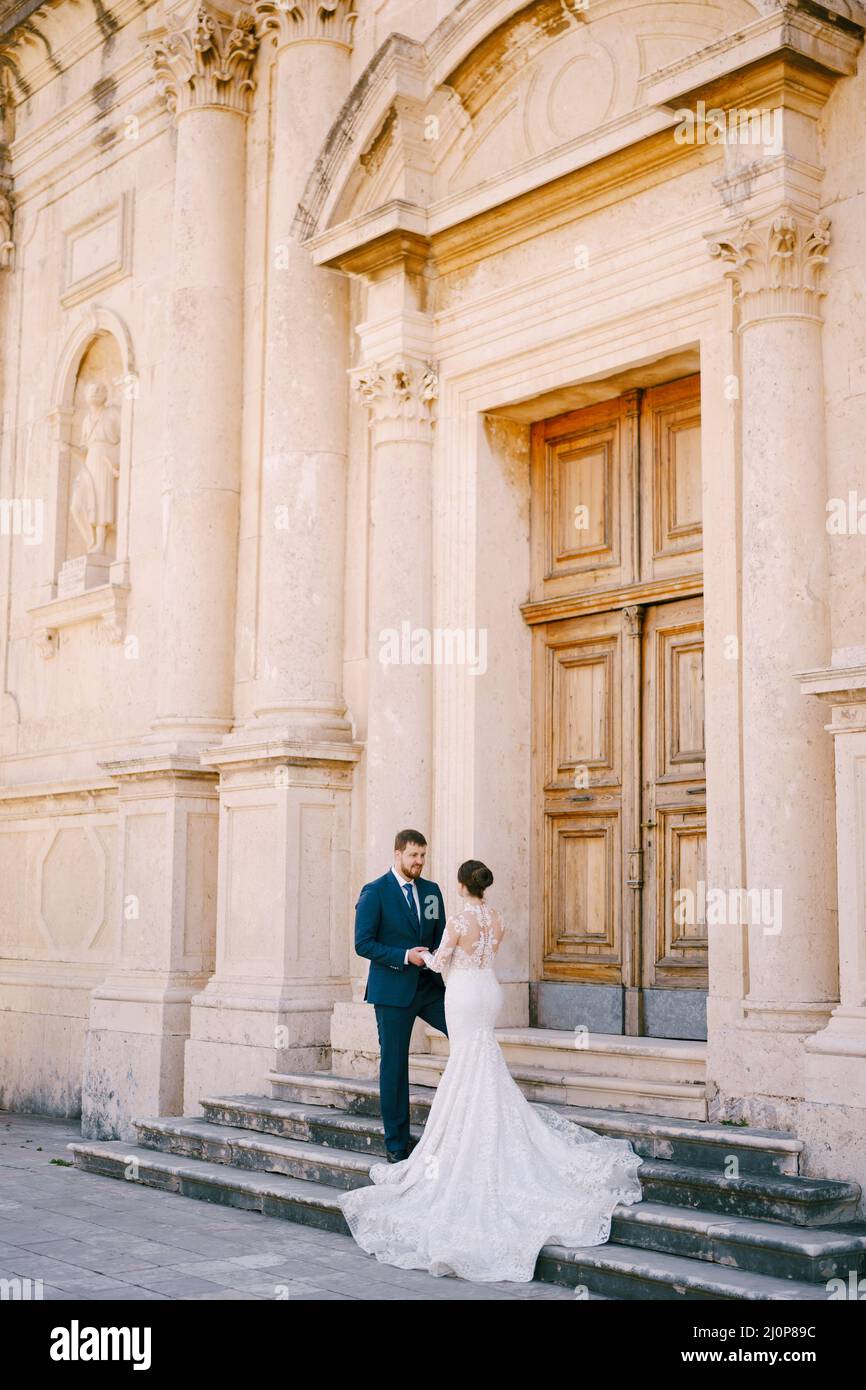 Bride and groom stand on the stone steps in front of the wooden door of ...
