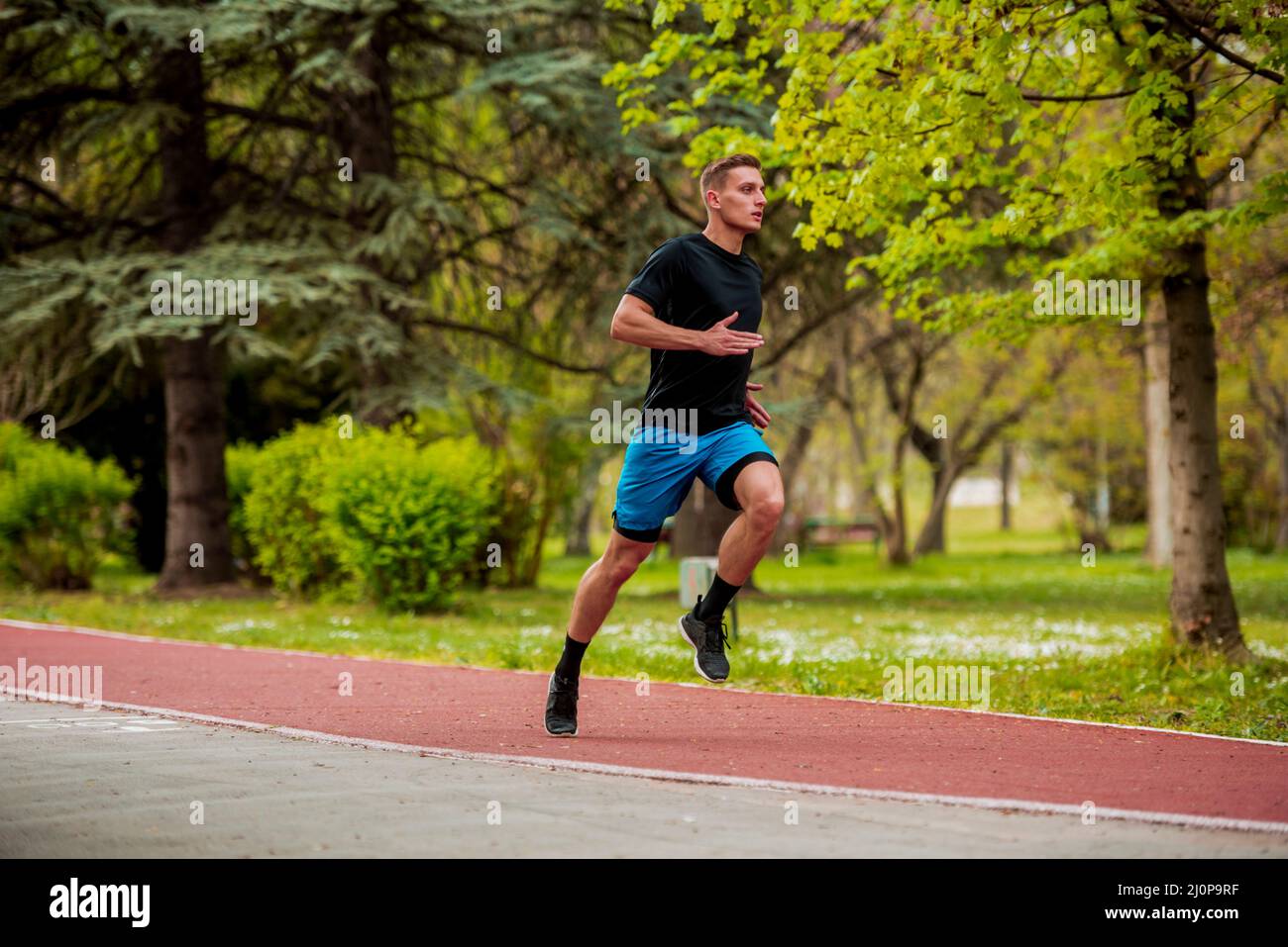 Attractive runner sprinting on the running track in city park area ...