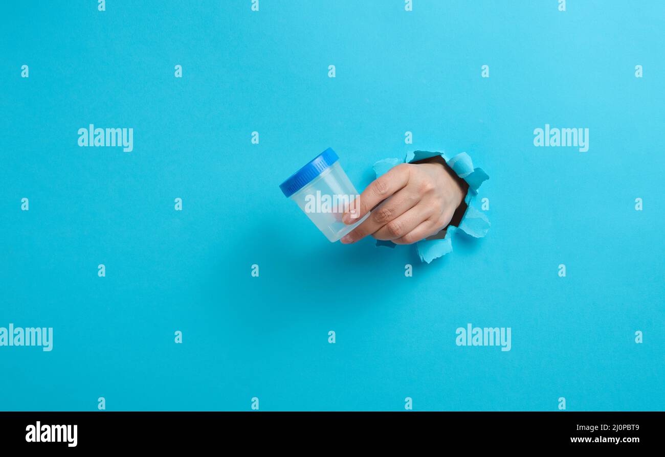 Female hand holds an empty plastic jar for urine tests, the hand is ...