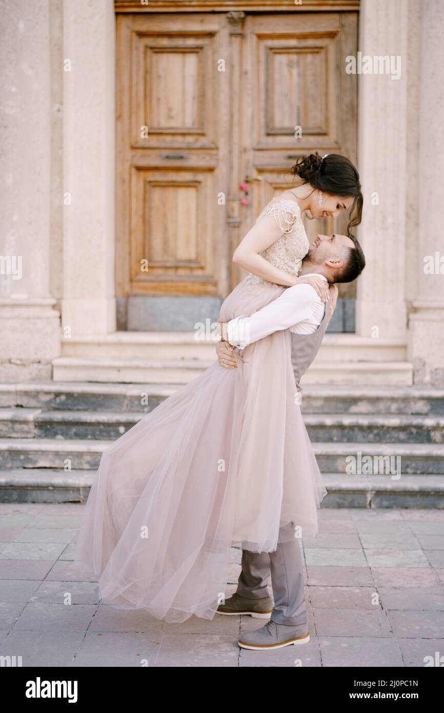 Groom holds bride in his arms in front of the entrance to the ancient ...
