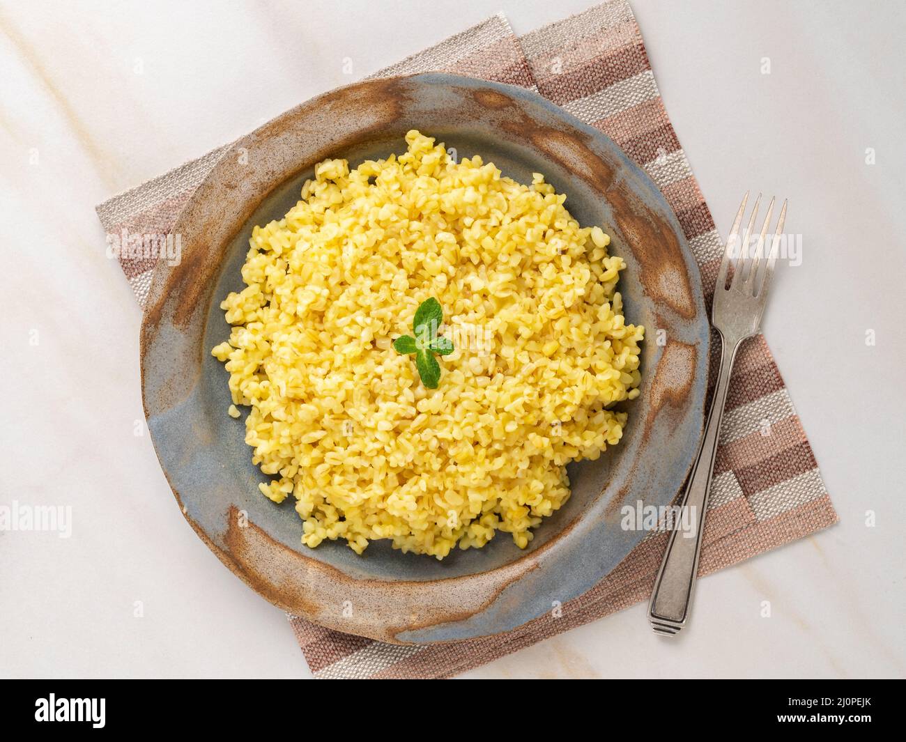 Bulgur wheat. Boiled bulghur cereal in plate on white marble table ...