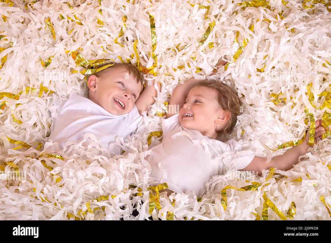A boy and a girl play in a pile of cut white and gold paper Stock Photo ...