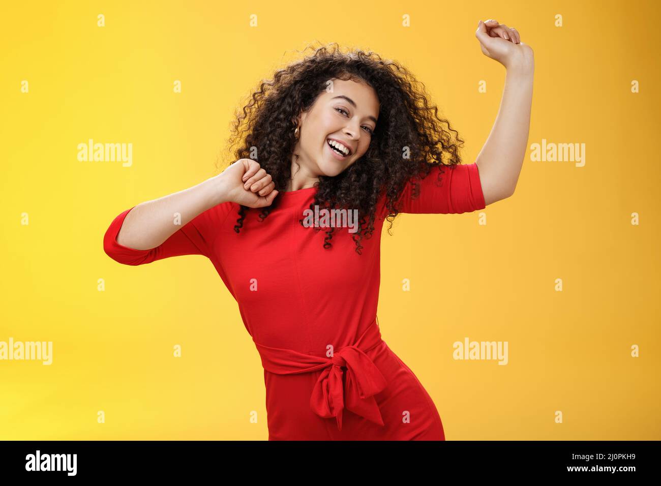 Carefree girl feeling uplifted and joyful dancing in red dress raising ...