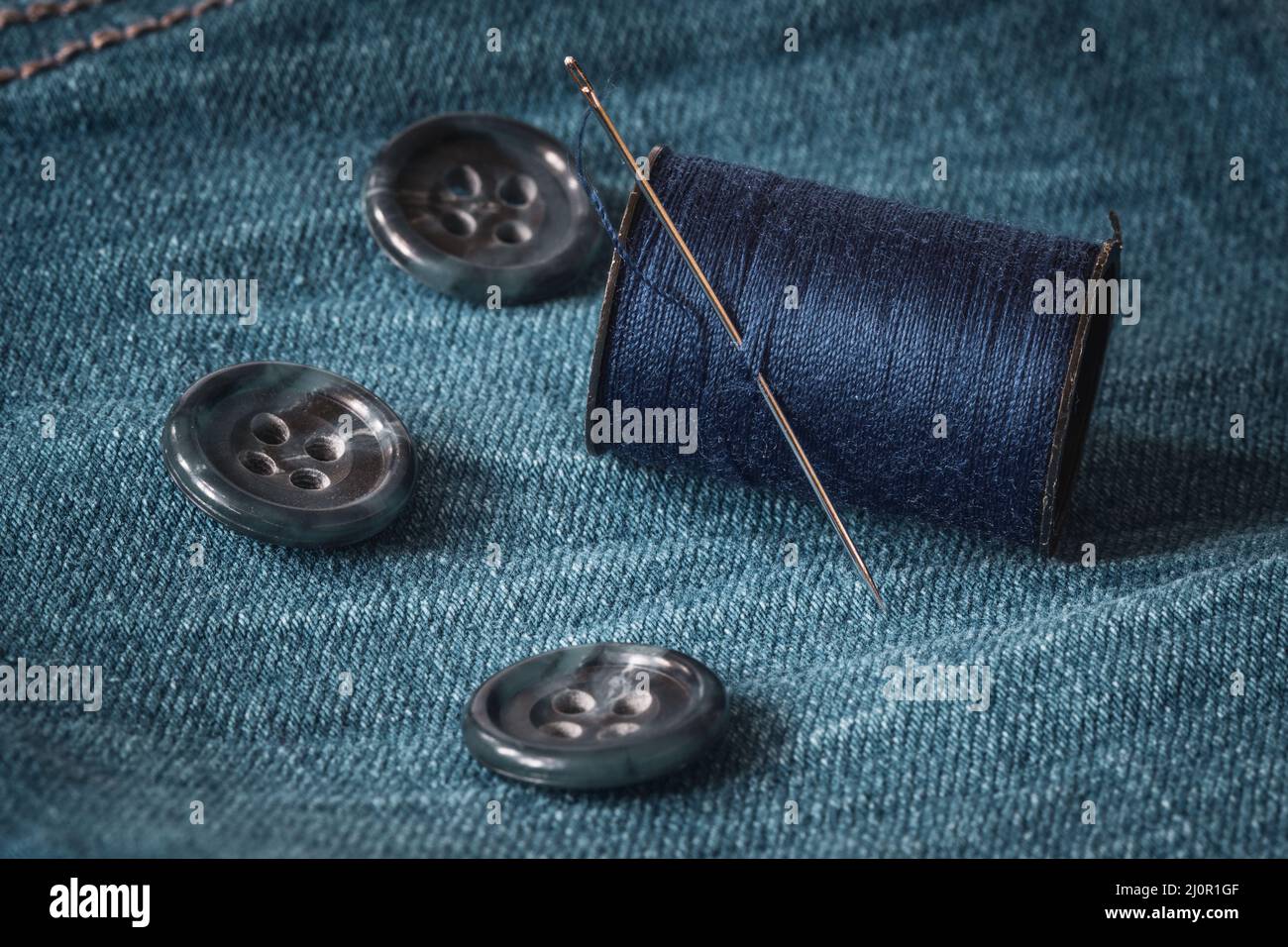 Needle and spool of thread on jeans fabric Stock Photo - Alamy