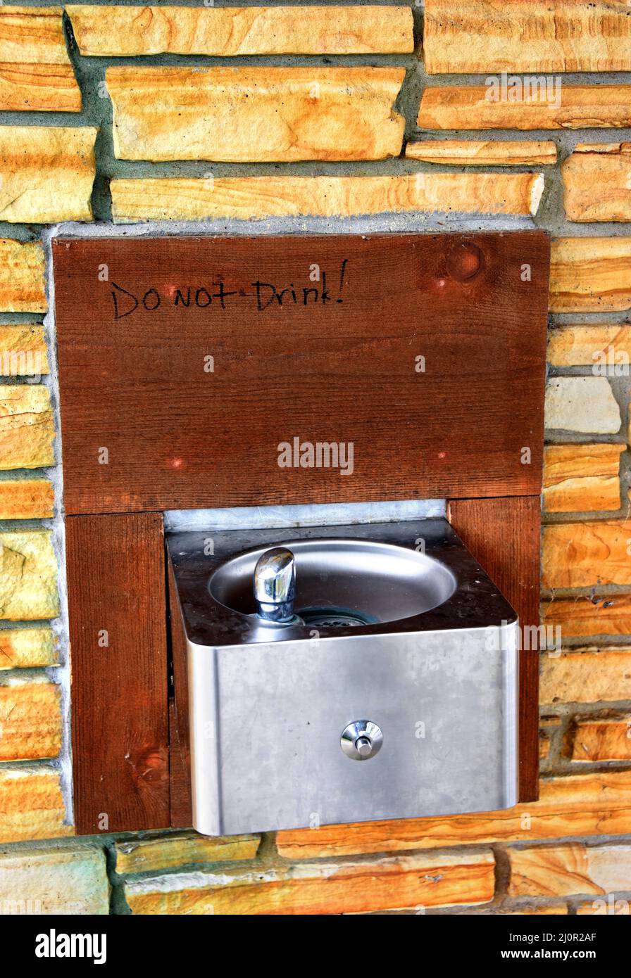 Rustic framed water fountain has hand written sign above it stating "Do ...