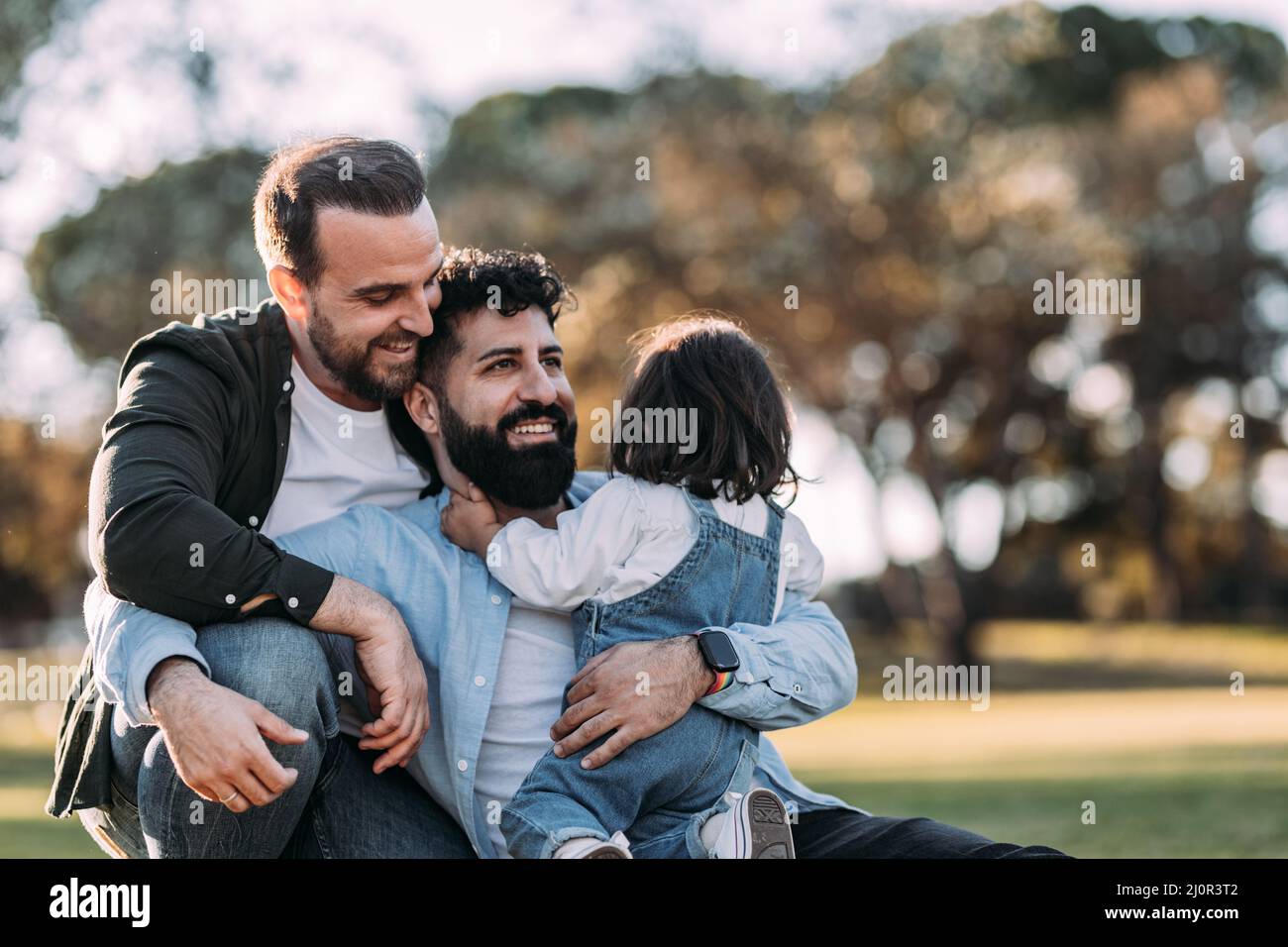 Male gay family embracing and happy in the park with their little ...