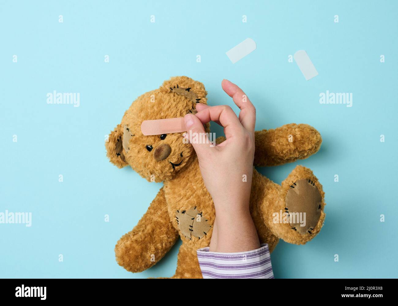 Female hand holds a brown teddy bear and glues a medical adhesive ...