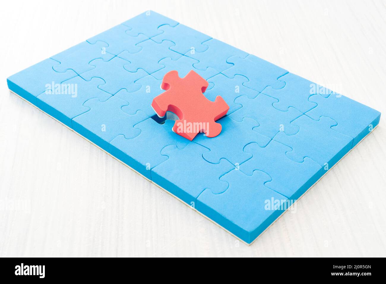 Red color puzzle piece standing out from larger group of blue puzzle ...