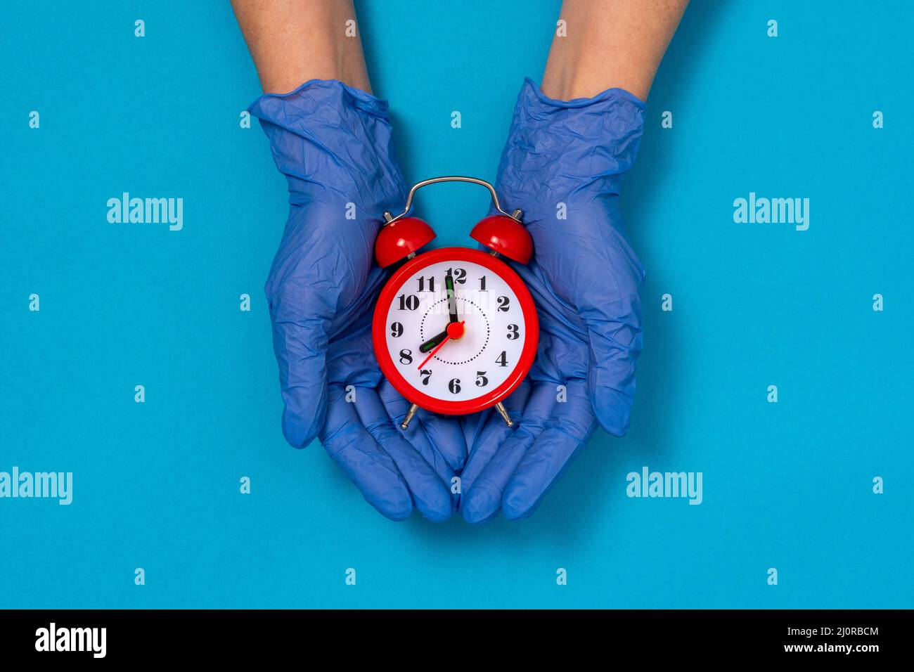 Hands in medical gloves holding red alarm clock Stock Photo - Alamy