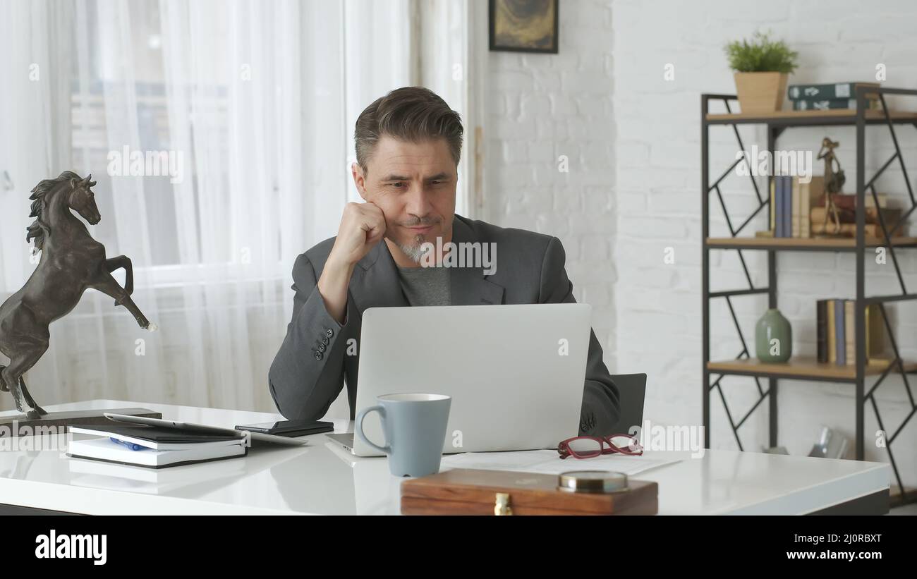 Older man working with laptop computer at home office, thinking ...
