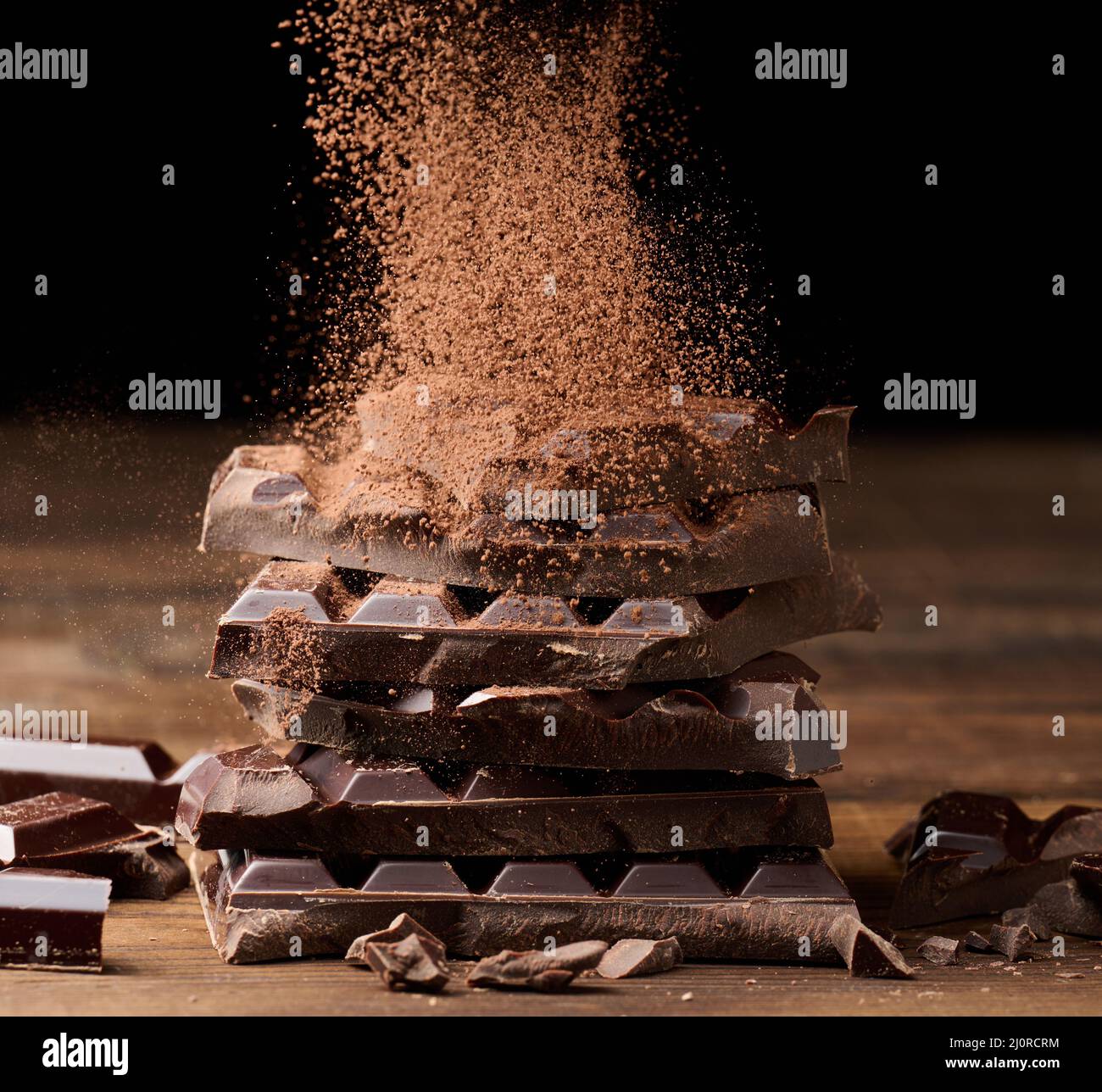 Cocoa powder sprinkles on a stack of broken dark chocolate on a wooden ...