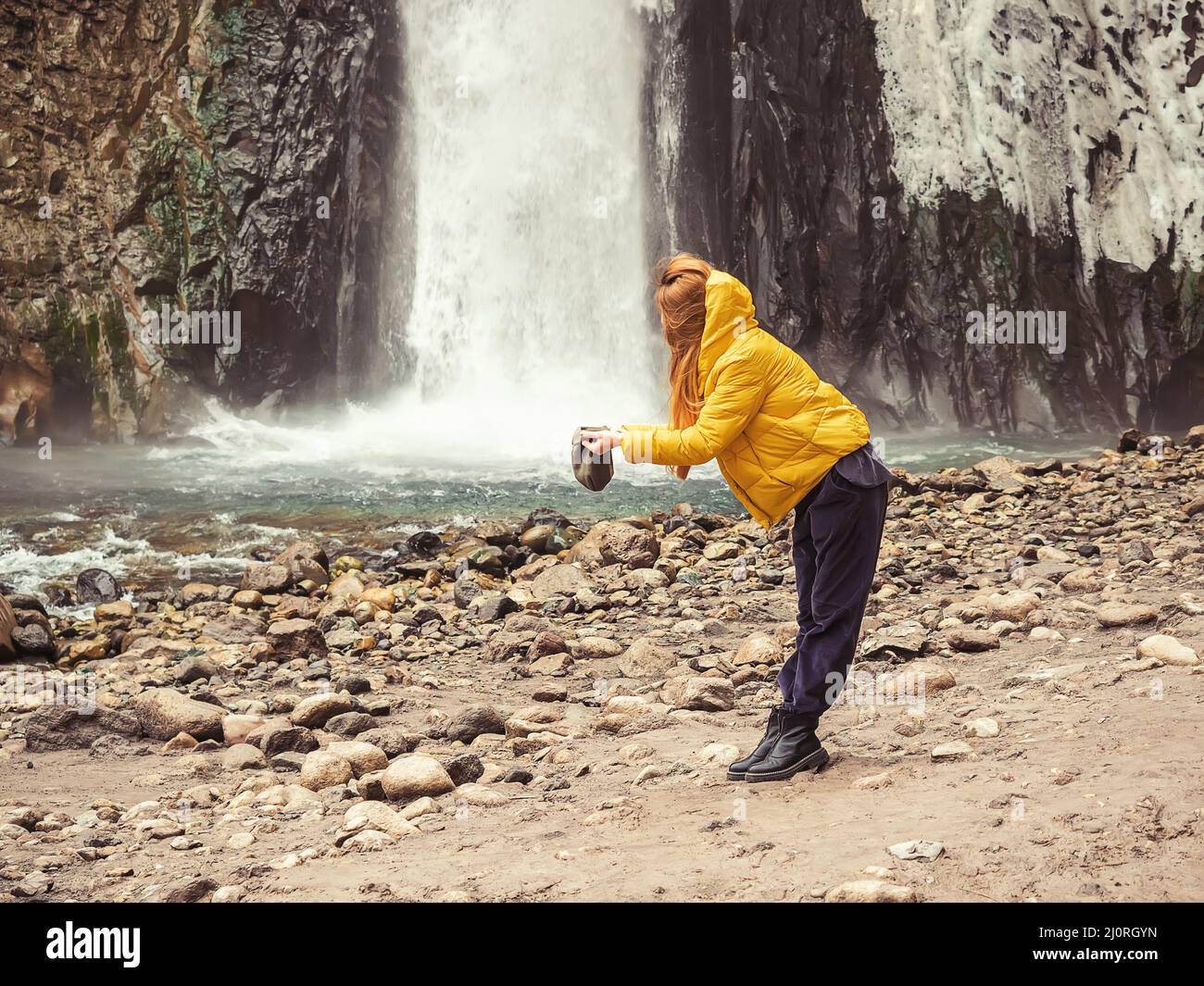 A woman stands against the backdrop of stormy waterfall flowing down ...