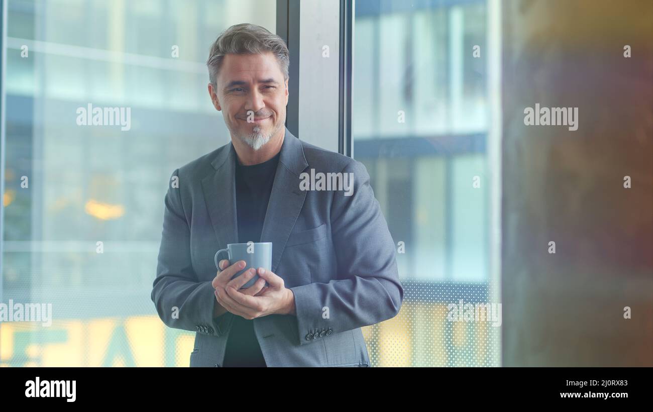 Happy older businessman taking break in office drinking coffee standing ...