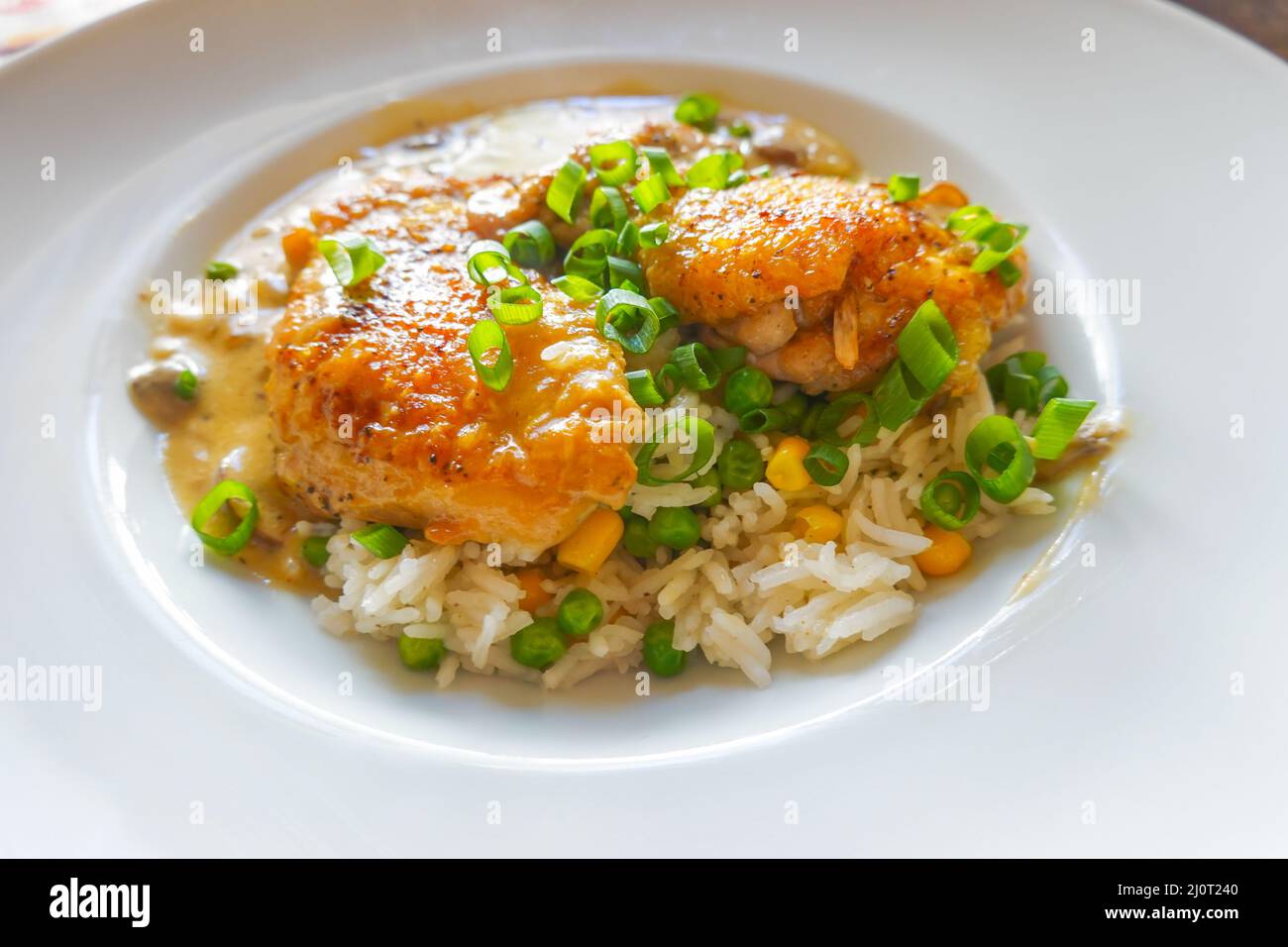 Sautéed boned chicken thighs on a bed of rice with peas and corn served ...