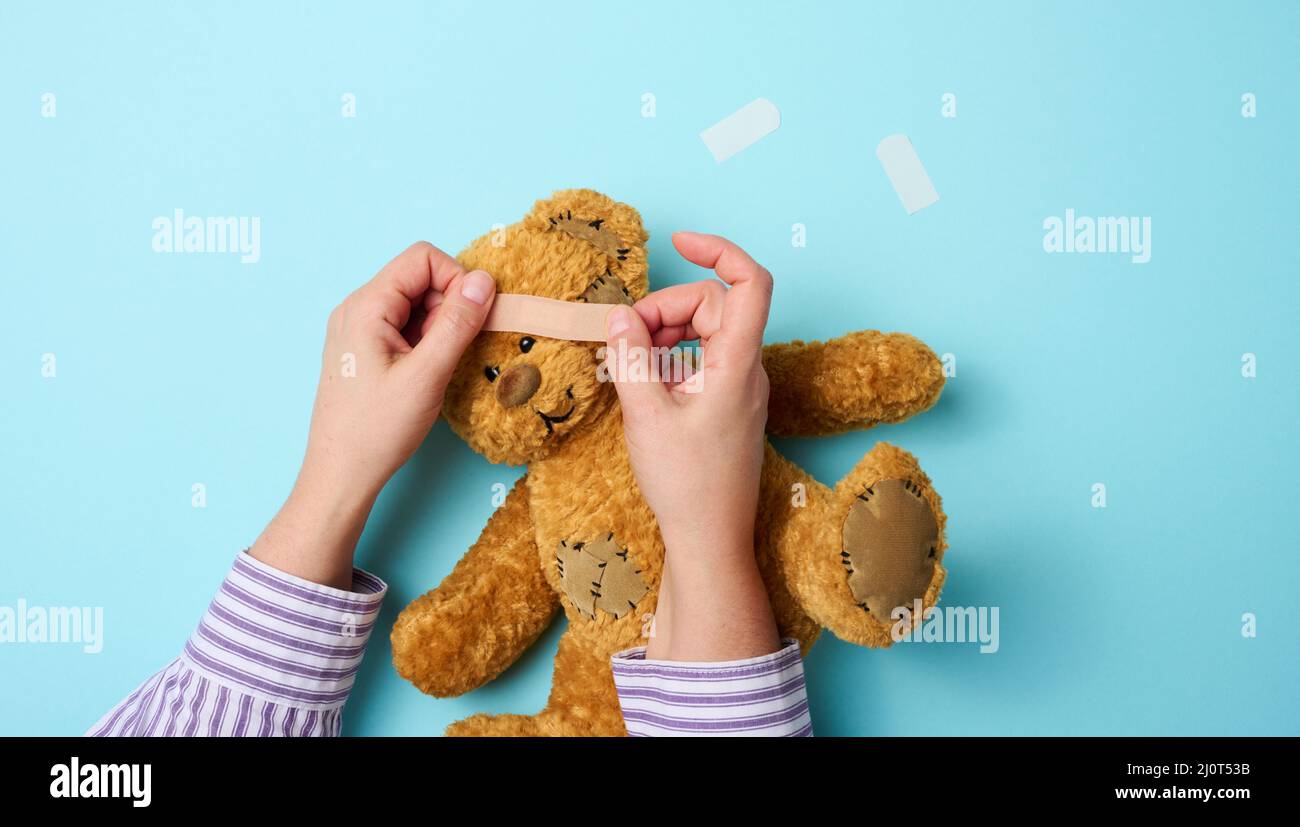 Female hand holds a brown teddy bear and glues a medical adhesive ...