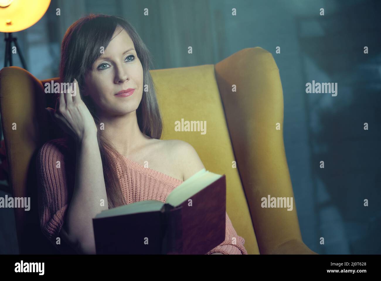 White Woman Reading Book At Home Sitting In Armchair In Cosy Room