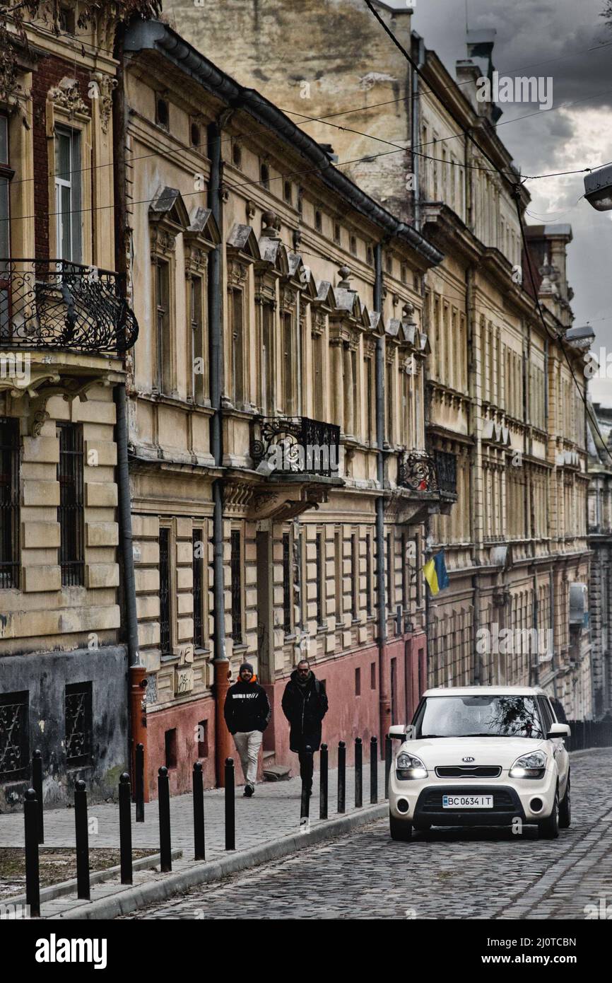 Car driving through a city with old buildings and people waking on the ...