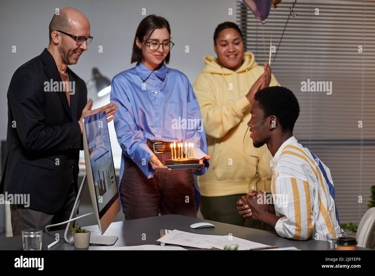 Diverse group of people bringing Birthday cake with candles to young ...