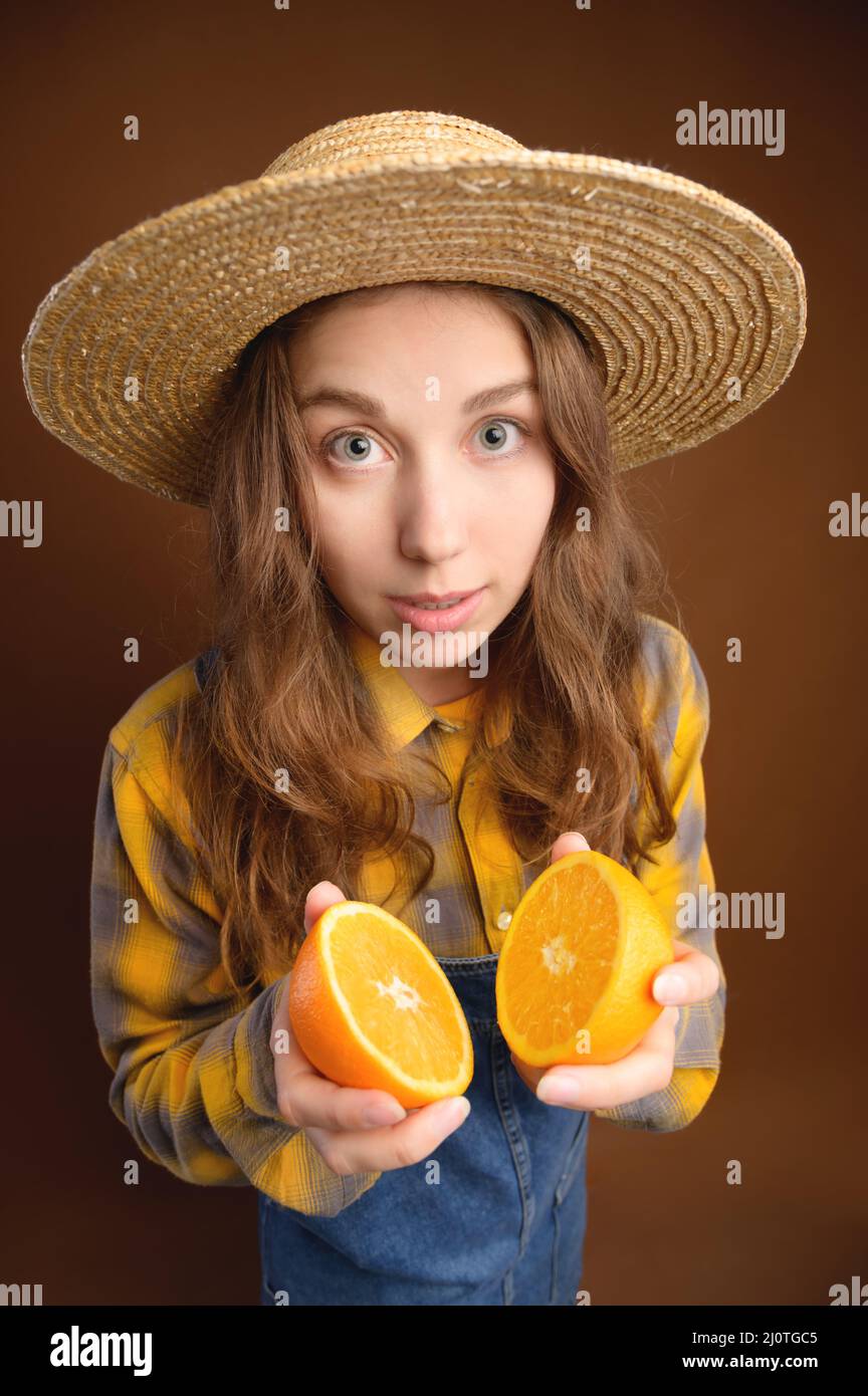 Surprised young woman looks at the camera and holds a cut orange in her ...