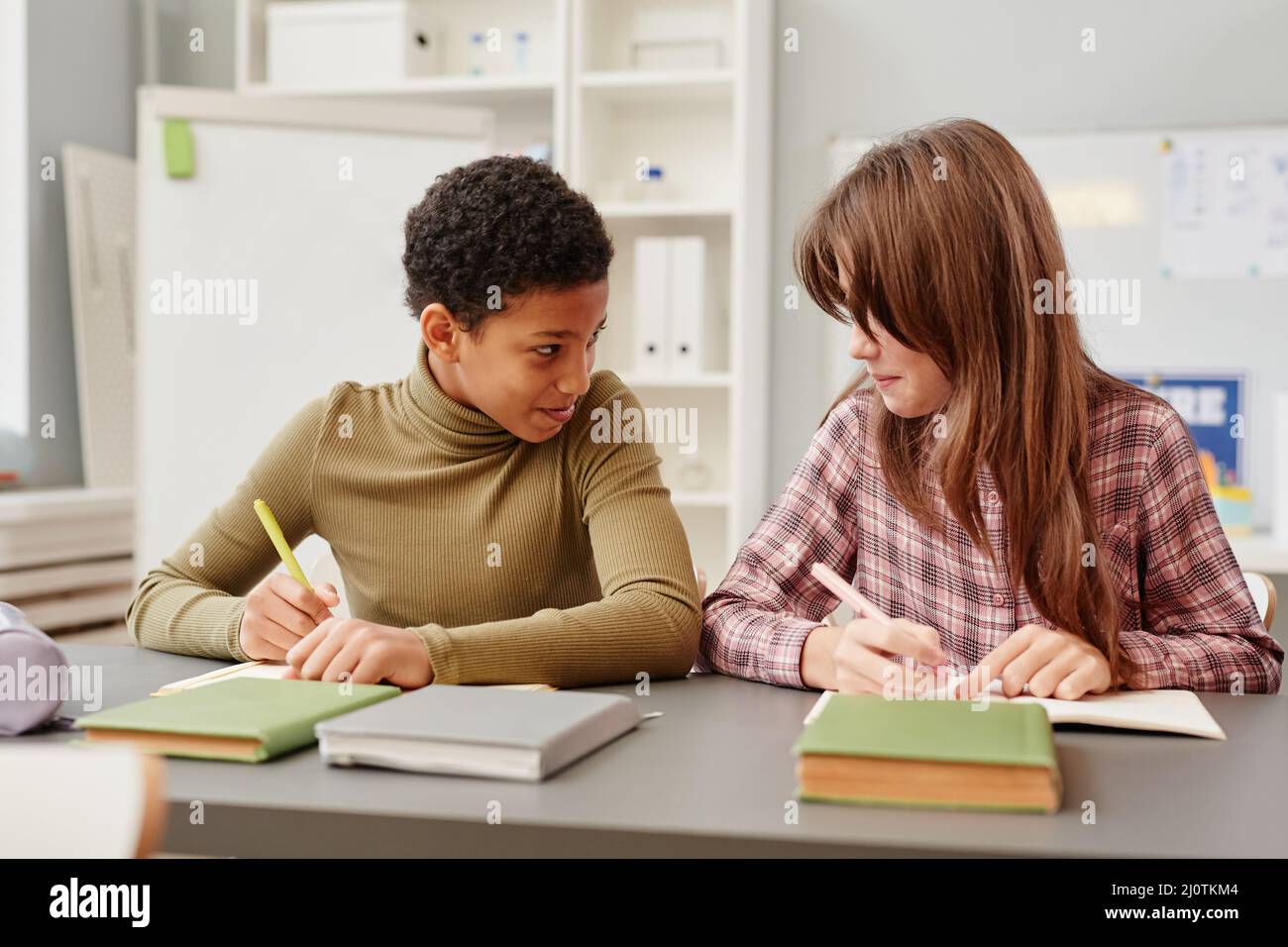 Portrait of two young girls whispering while cheating during test in ...