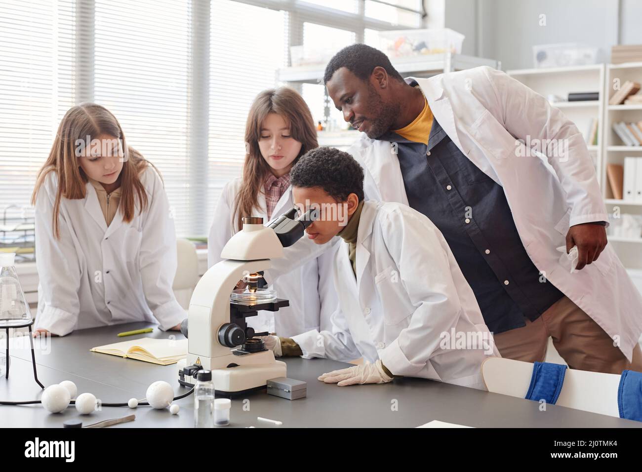 Side view portrait of young black girl looking into microscope with ...