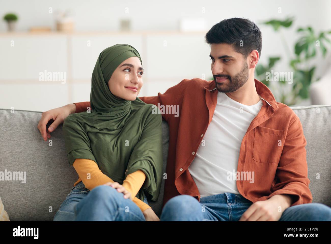 Happy Muslim Wife Wearing Hijab Looking At Husband Sitting Indoors ...