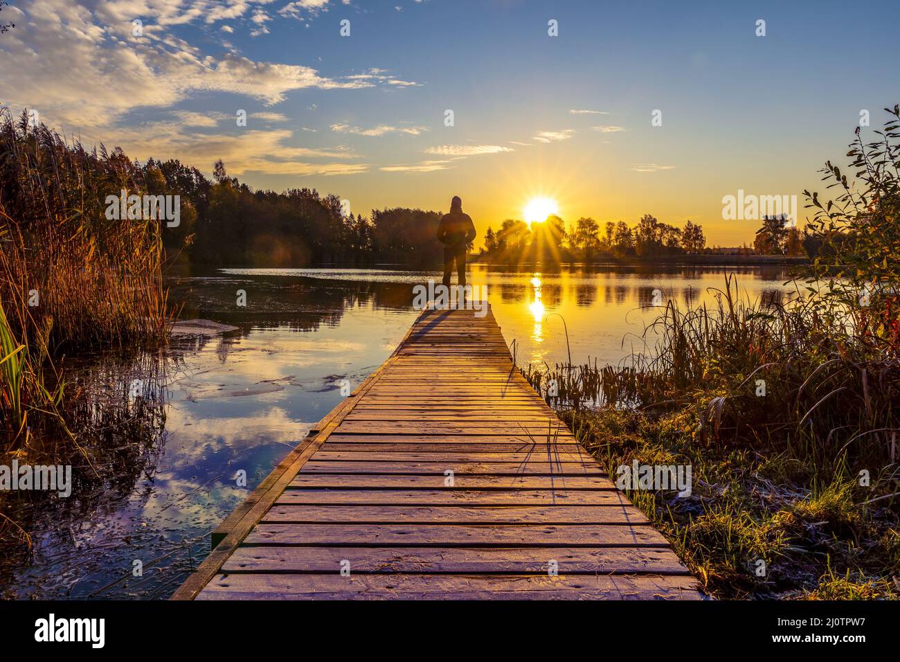 Silhouette of man standing on the lake wooden bridge facing to the ...