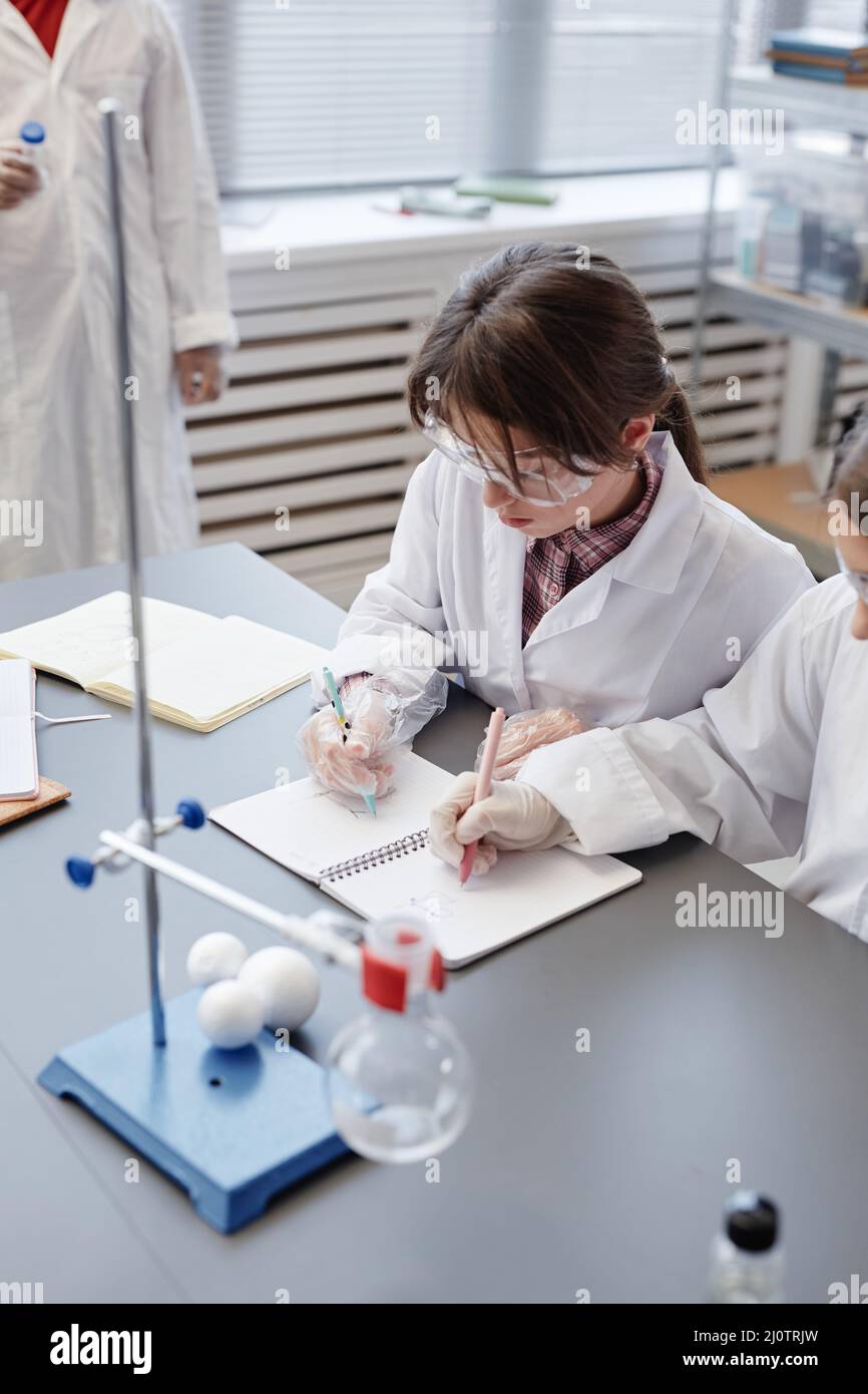 Vertical portrait of children taking notes while doing science ...