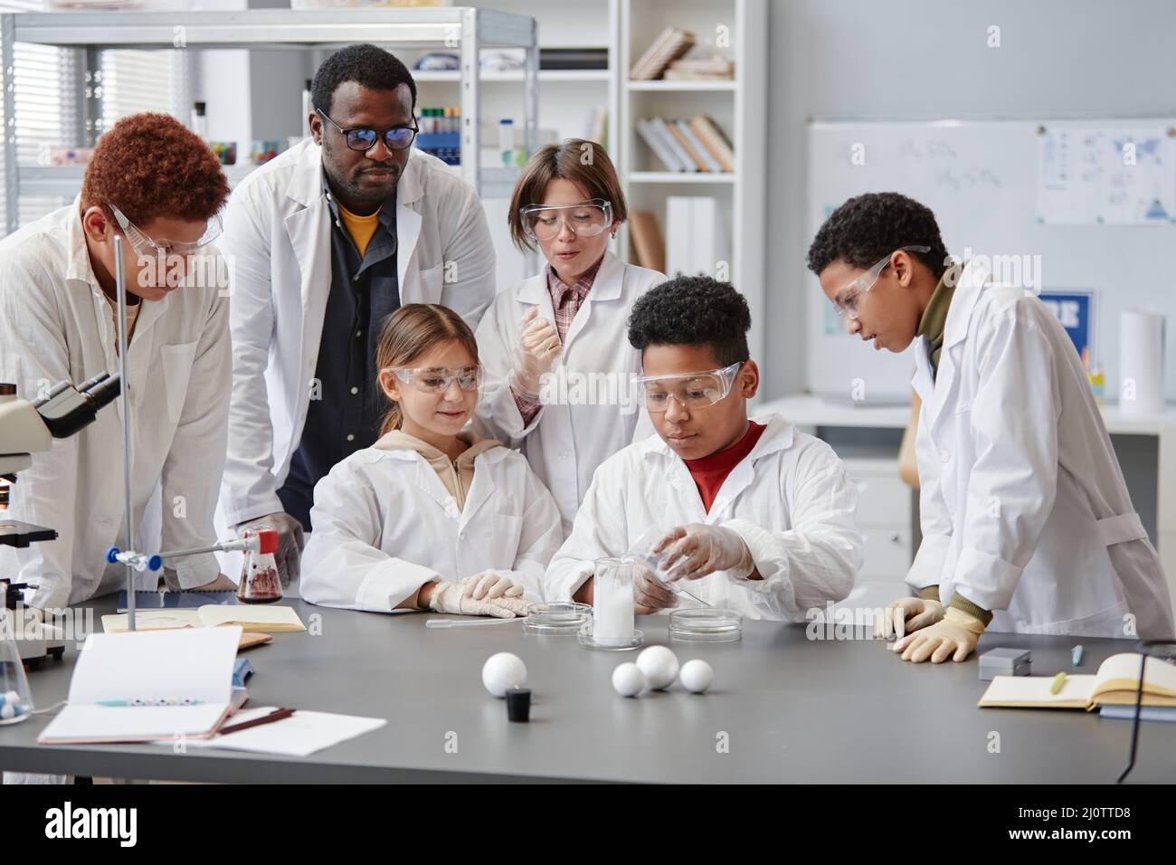 Diverse group of children wearing lab coats in chemistry class while ...