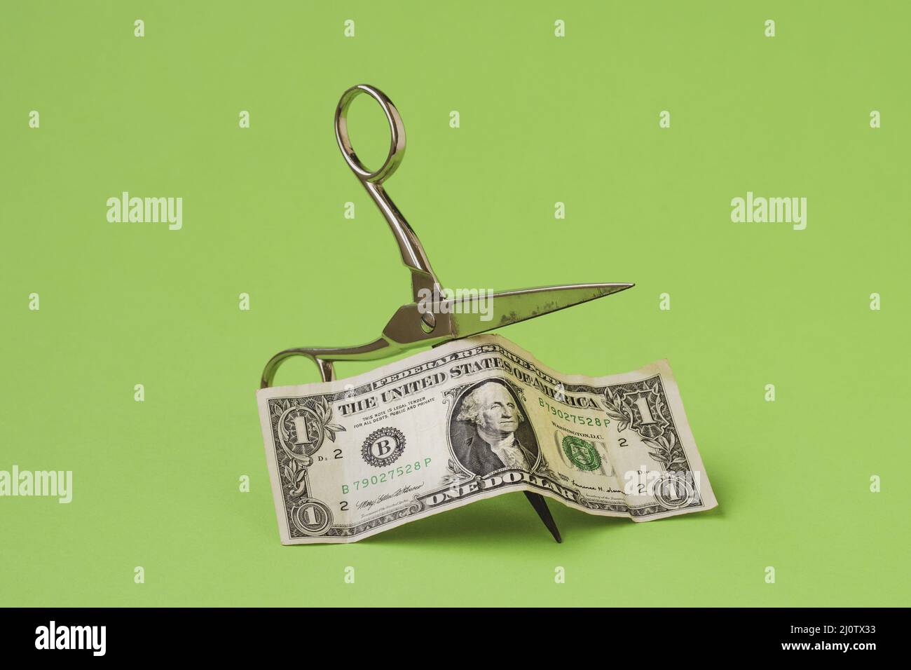 Cutting one dollar with scissors on green background Stock Photo - Alamy