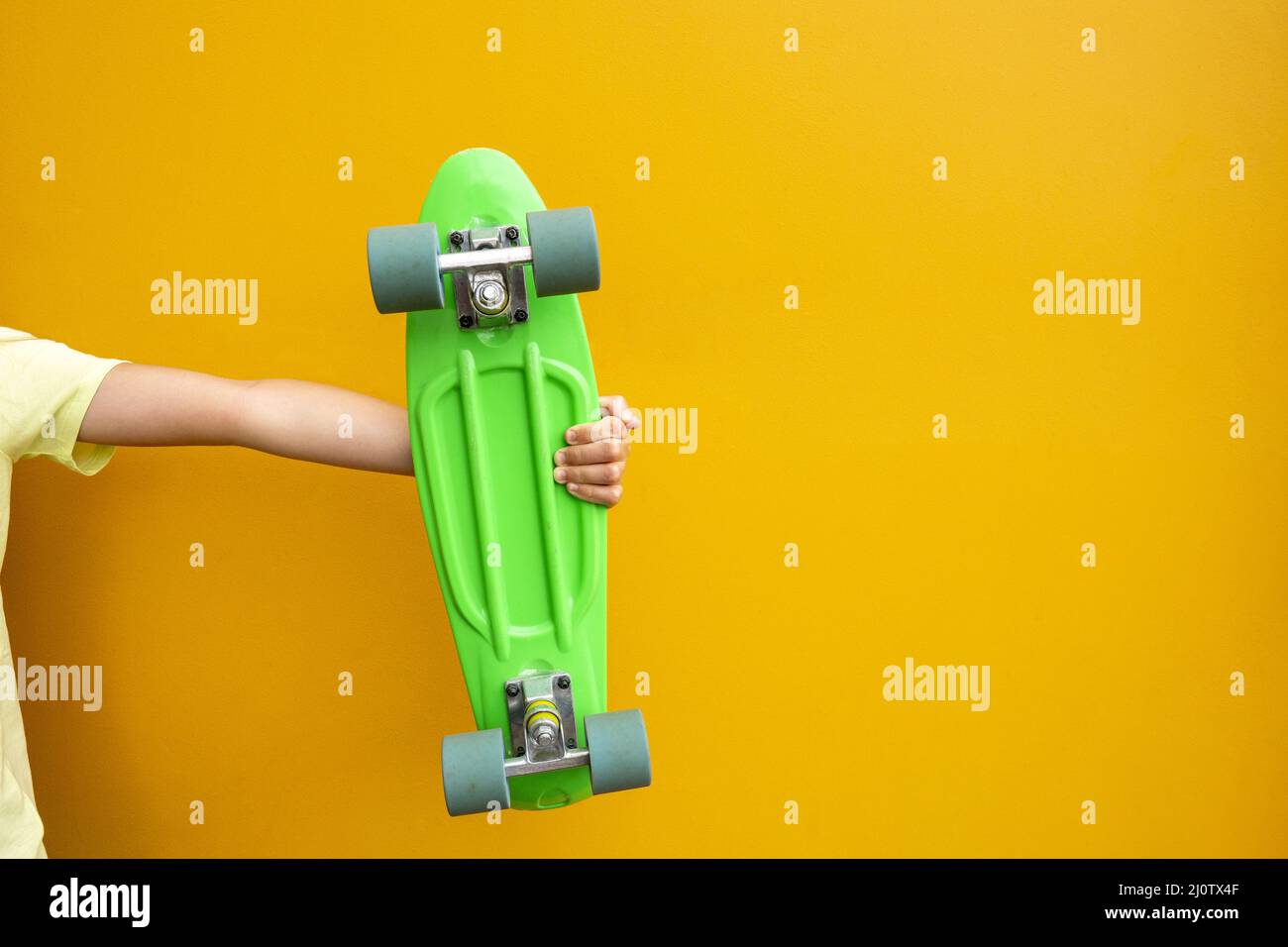 Hand with green penny board against yellow urban wall Stock Photo - Alamy