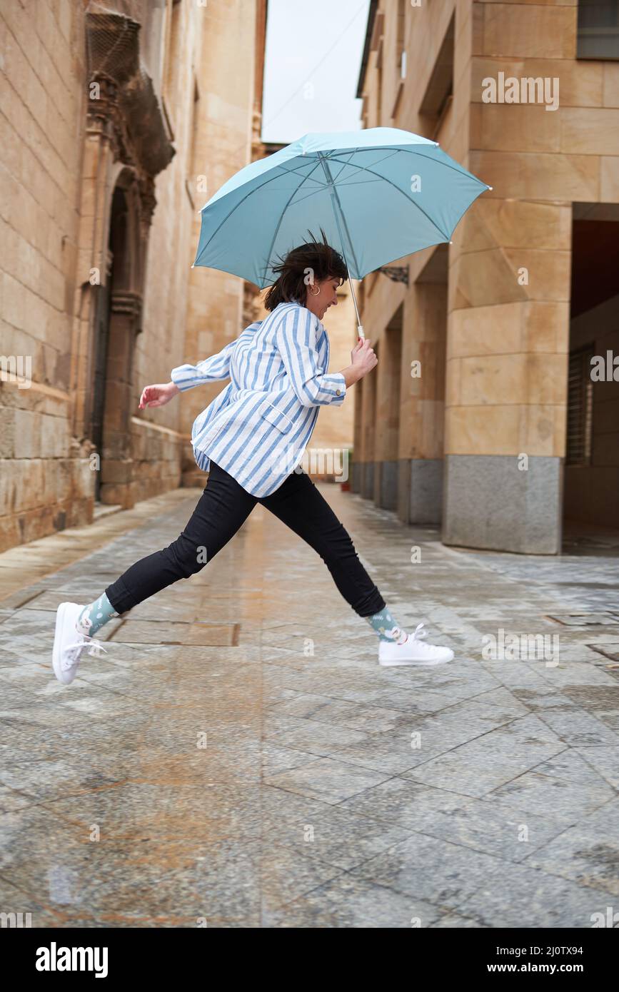 Woman jumping over a puddle on a rainy day Stock Photo - Alamy
