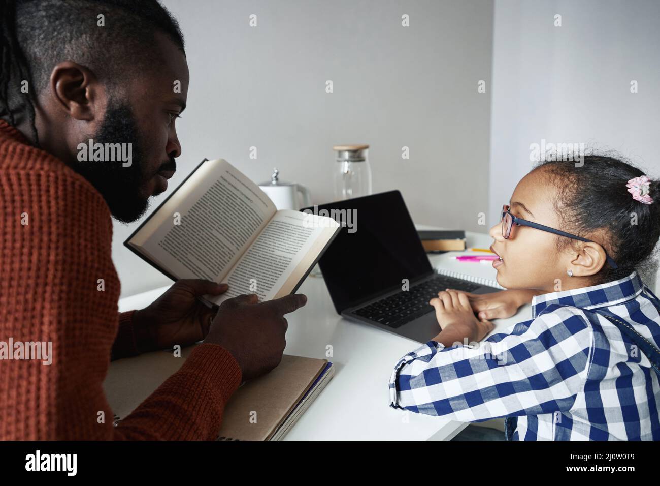 Young girl listening intently to her father as he reading book Stock ...