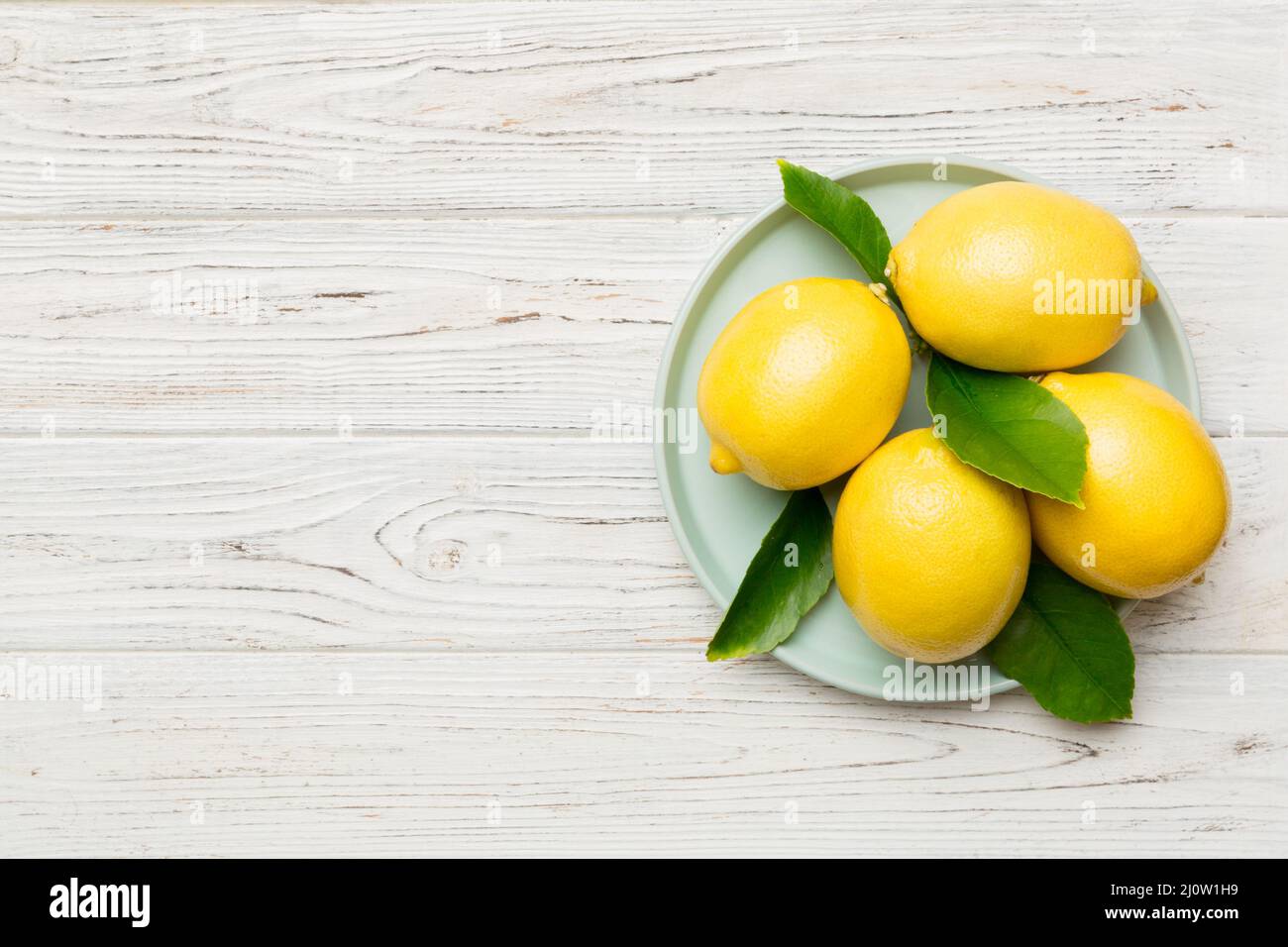 Fresh cutted lemon and whole lemons over round plate on colored ...