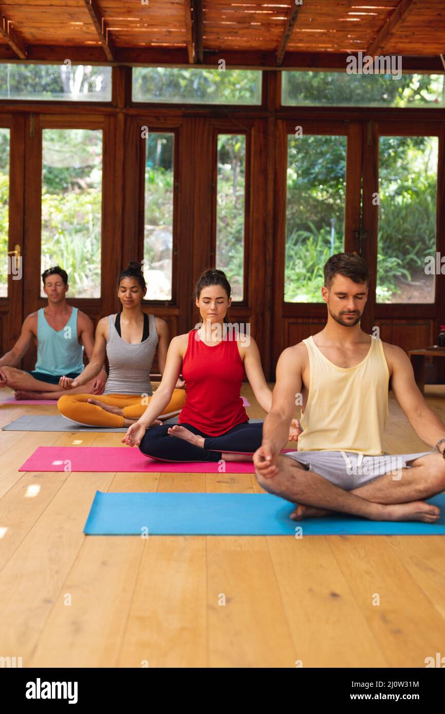 Men and women meditating while sitting on exercise mats at health club ...