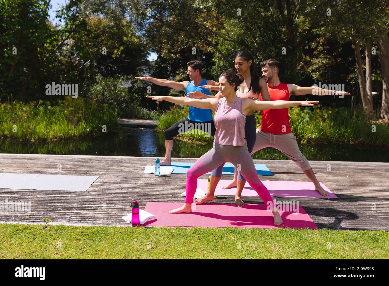 Female yoga instructor assisting woman and men in exercising at park ...