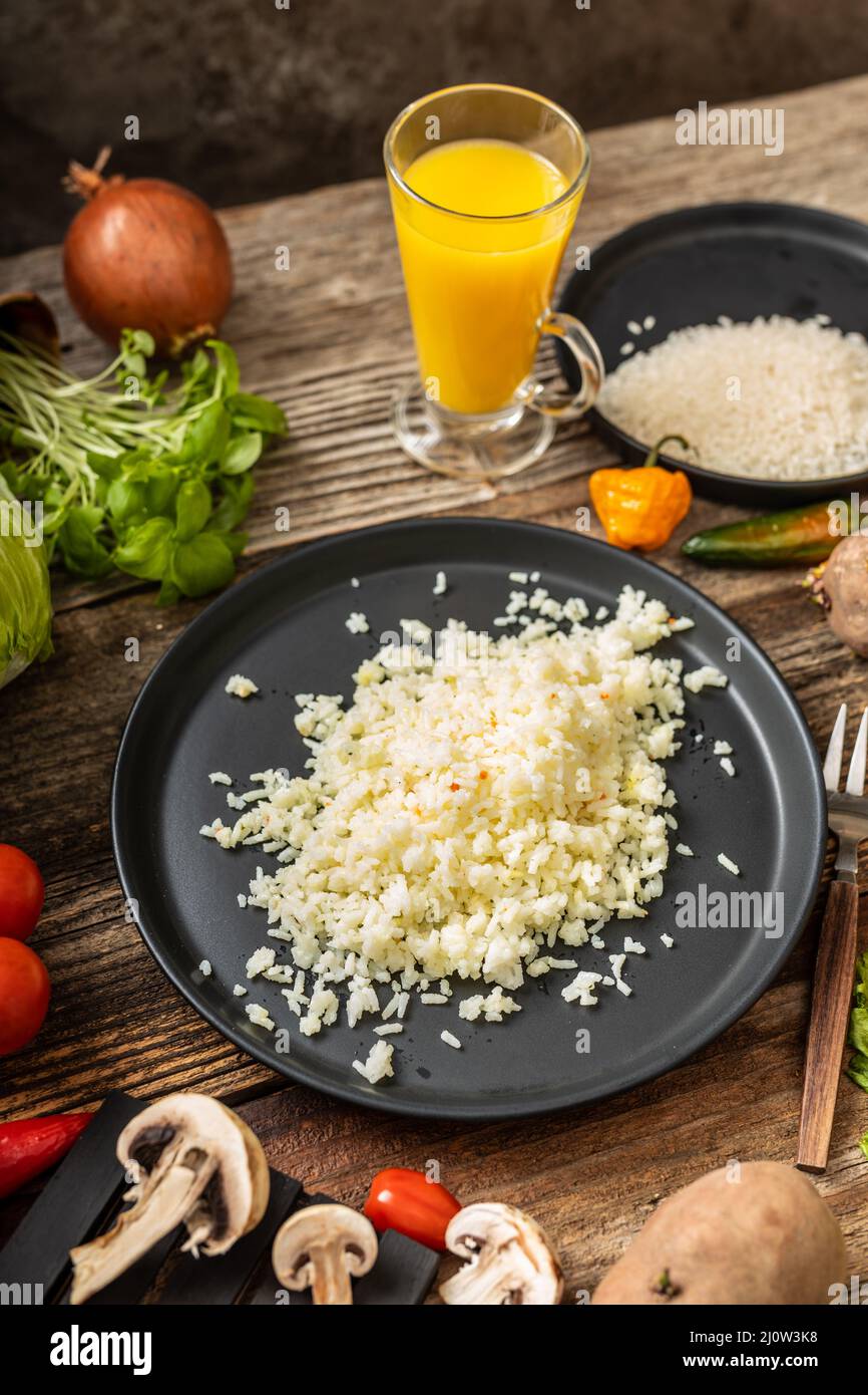 Rice garnish on black plate around vegetables Stock Photo - Alamy