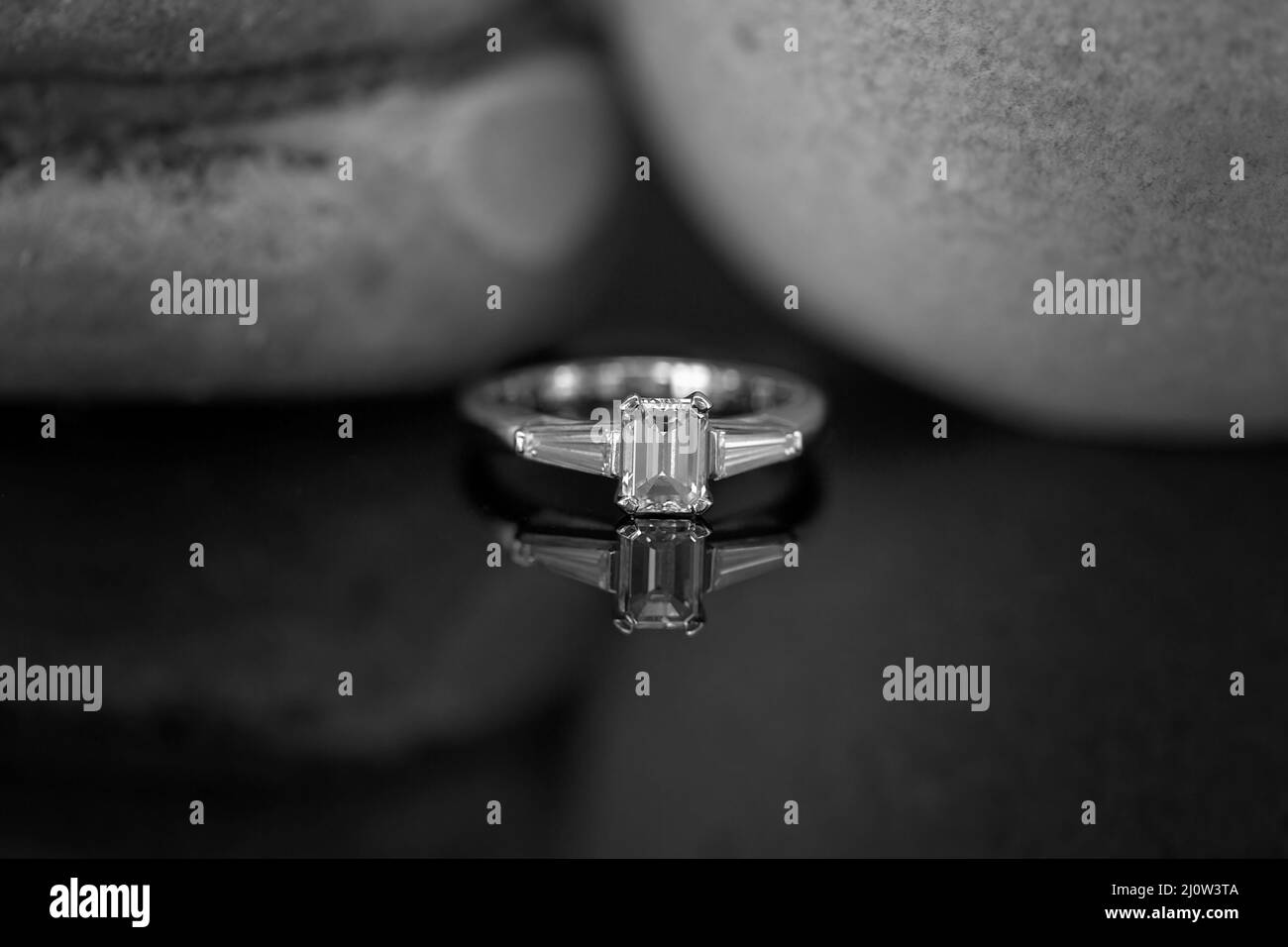 An emerald cut diamond ring on a black surface with reflections ...