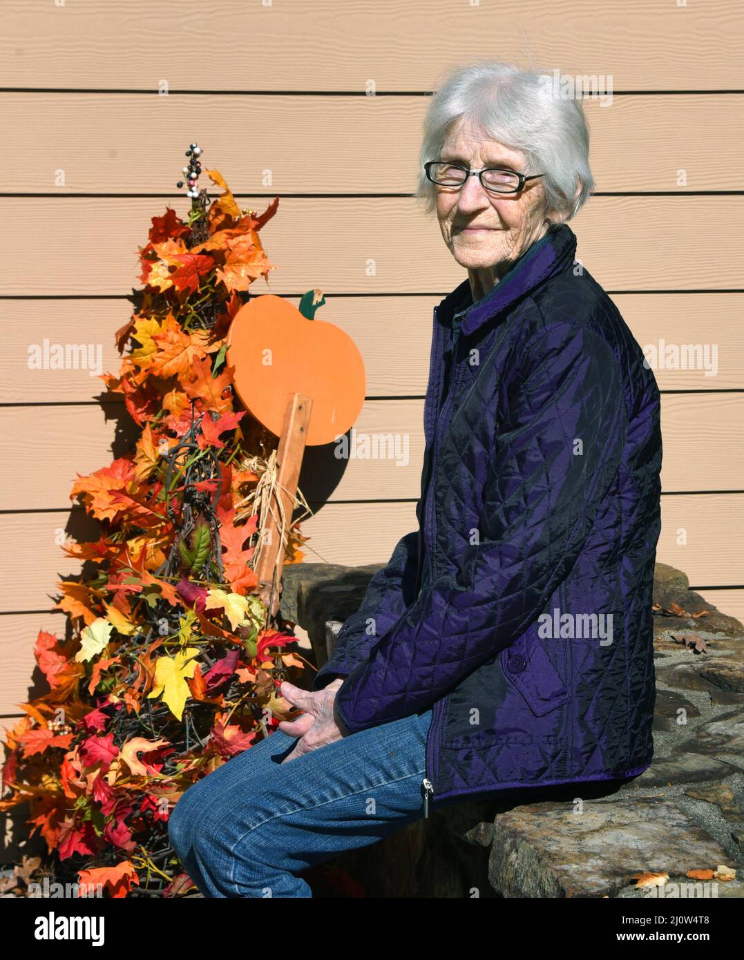 Elderly woman enjoys the sunshine of a Fall day as she sits outside her ...
