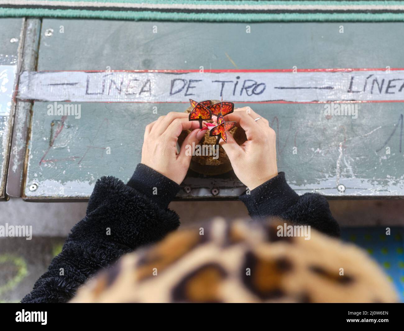 Hands of a girl sticking darts into a cork on the shooting line of a ...