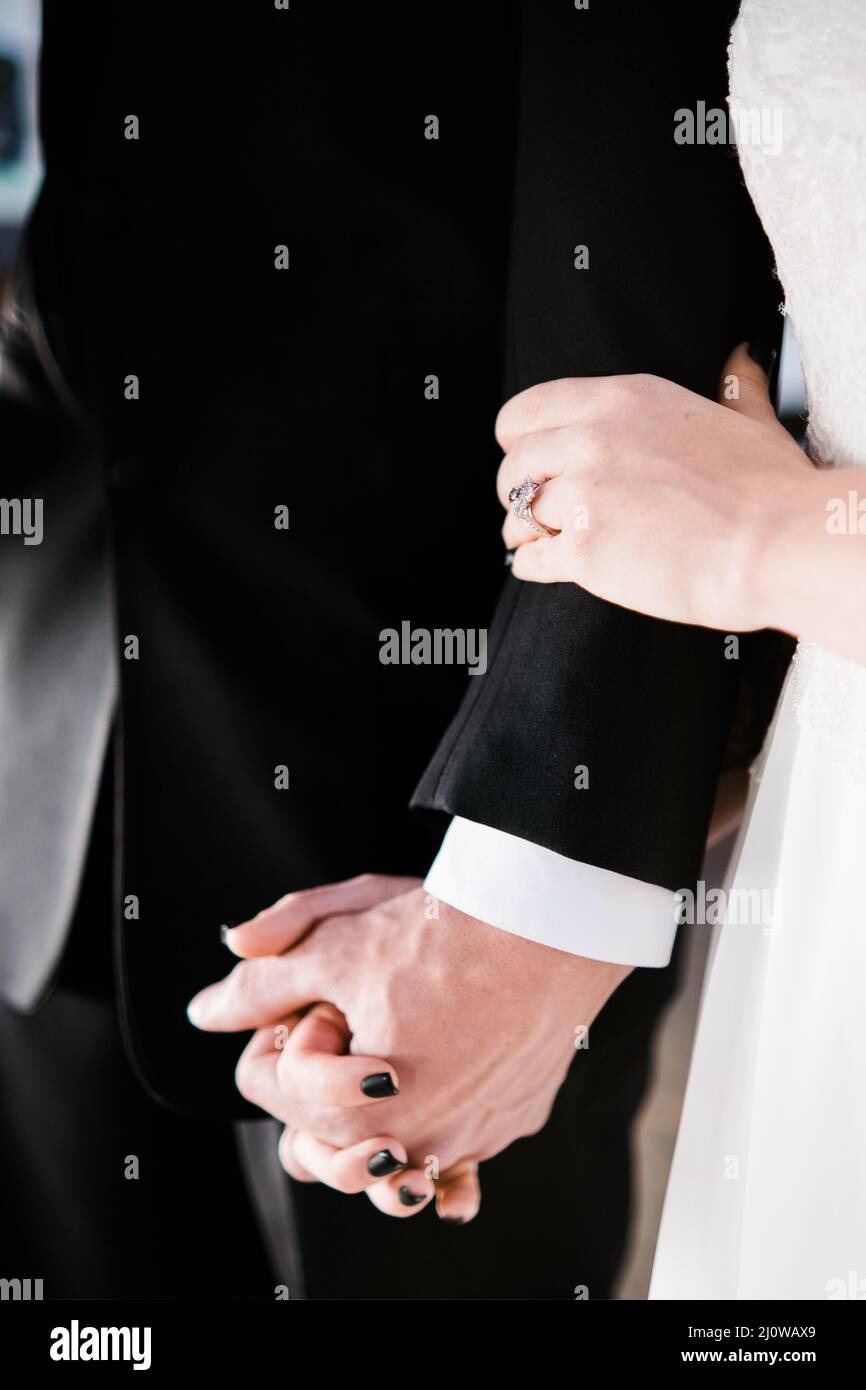 Vertical closeup shot of a bride and groom holding hands on their ...