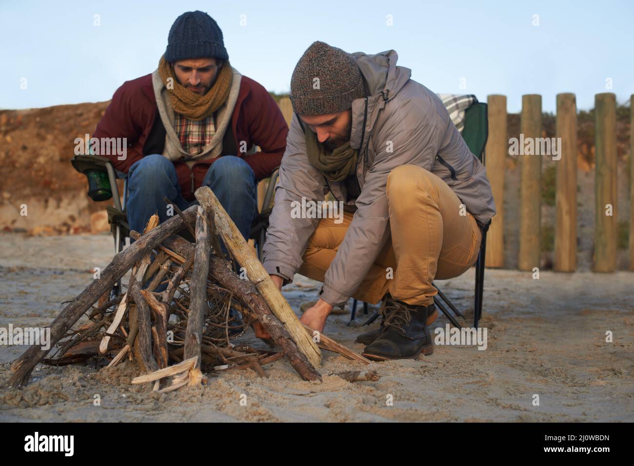 Lets get this a blazing. Two young men building a fire on the beach ...