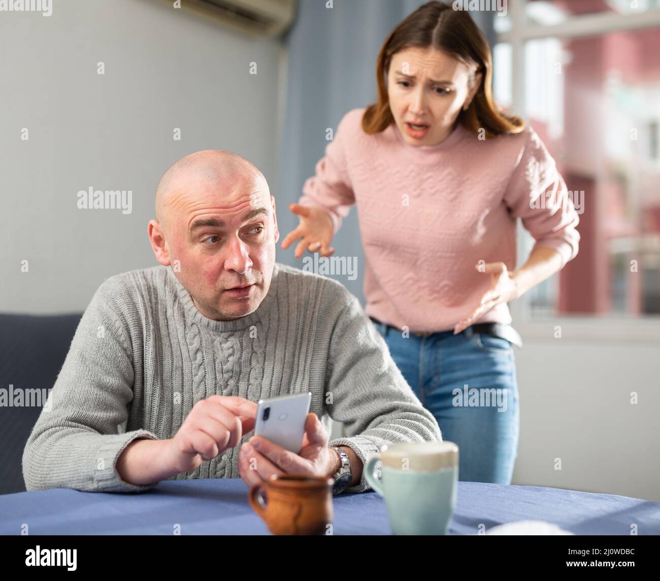 Man is texting on a mobile phone, while woman is outraged Stock Photo ...