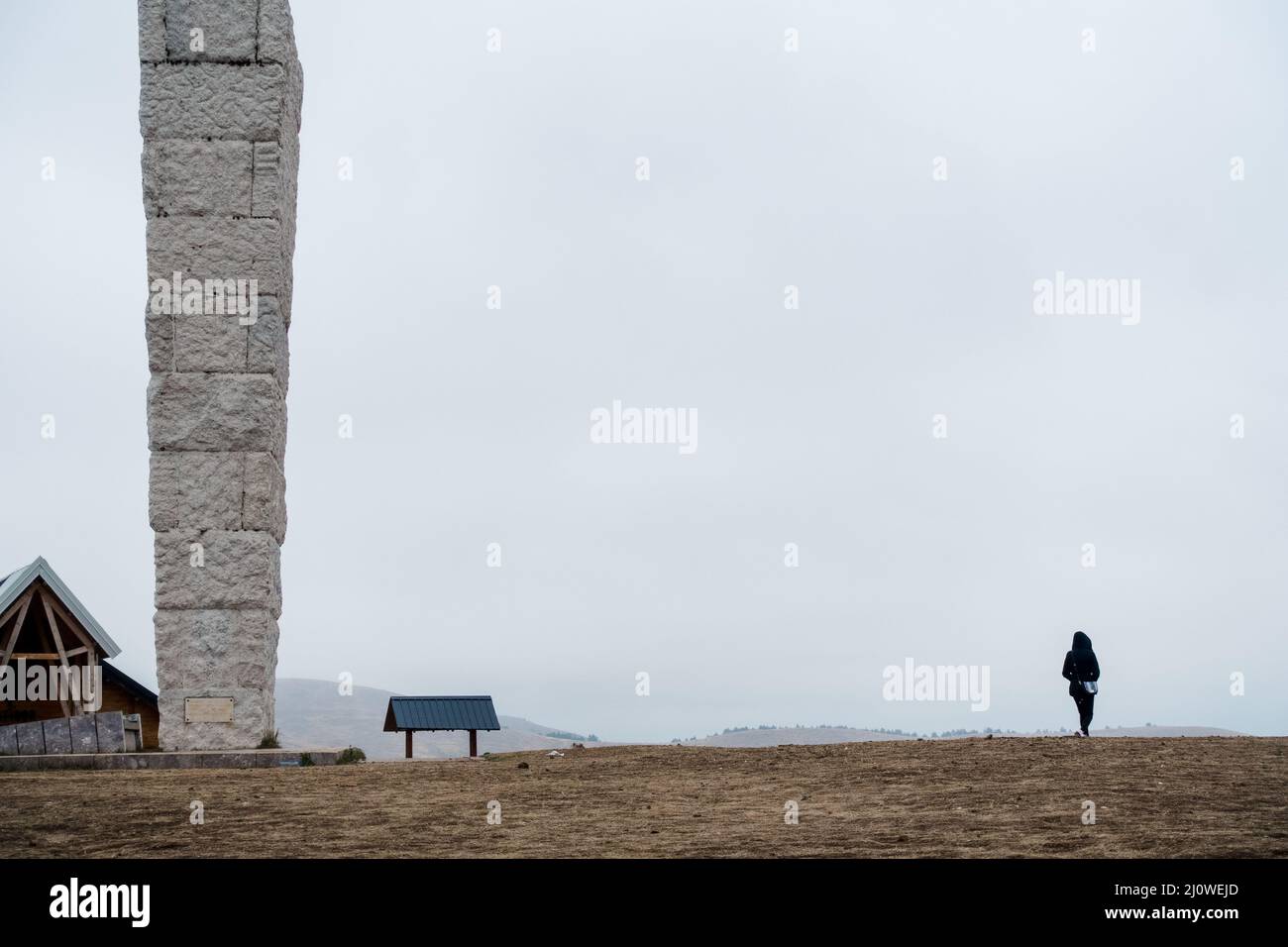 Rear view of a female standing on field parallel to a brick monument ...