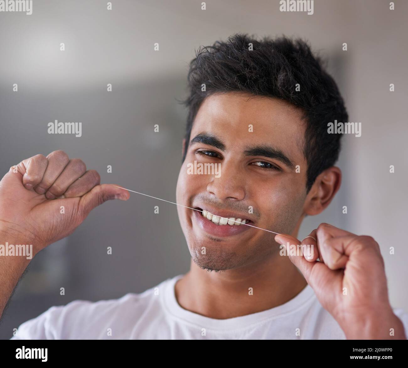Keeping it clean in the spaces in between. Portrait of a happy young man flossing his teeth at ...