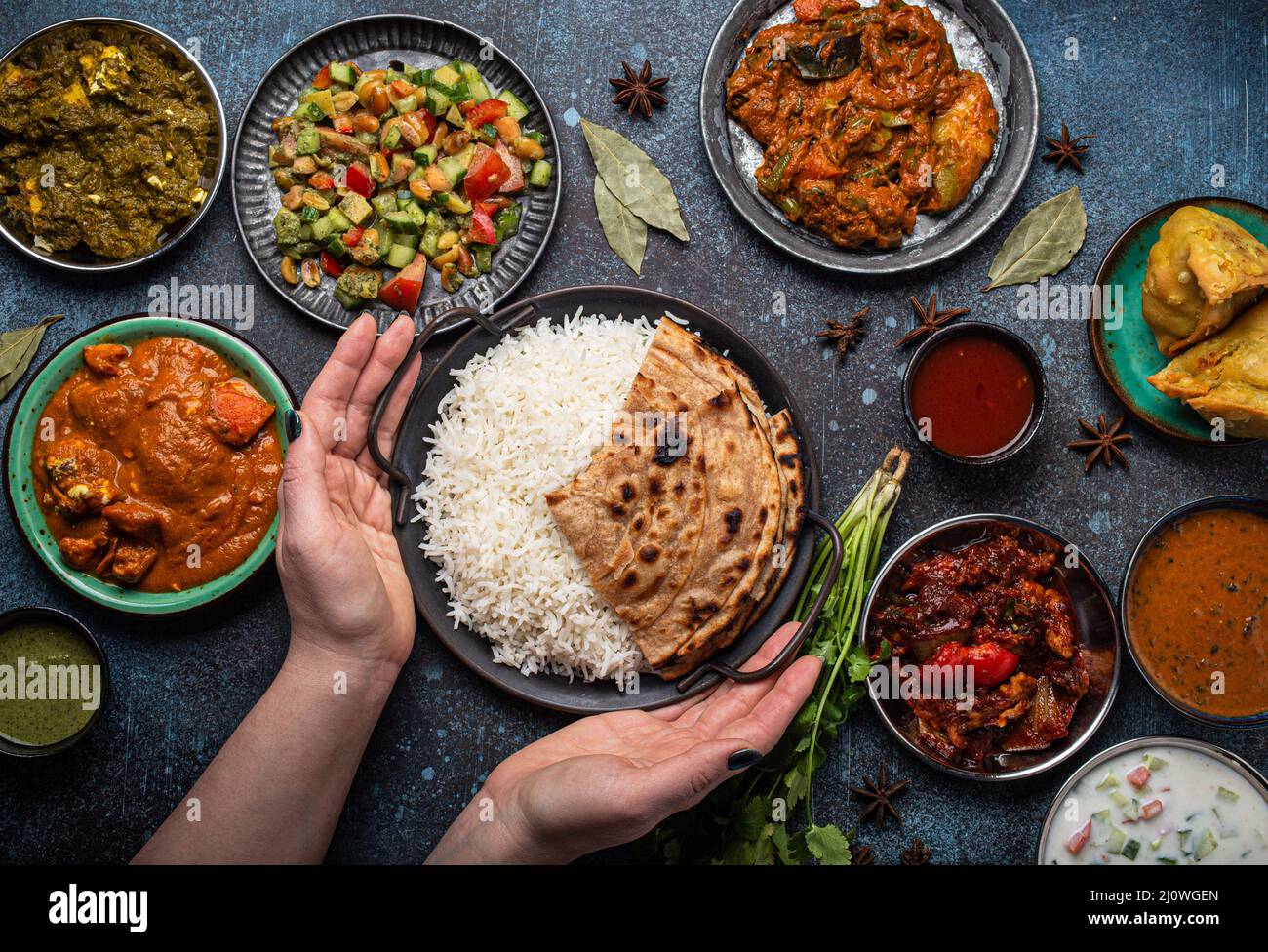 Female hands serving Indian ethnic food buffet on rustic concrete table ...