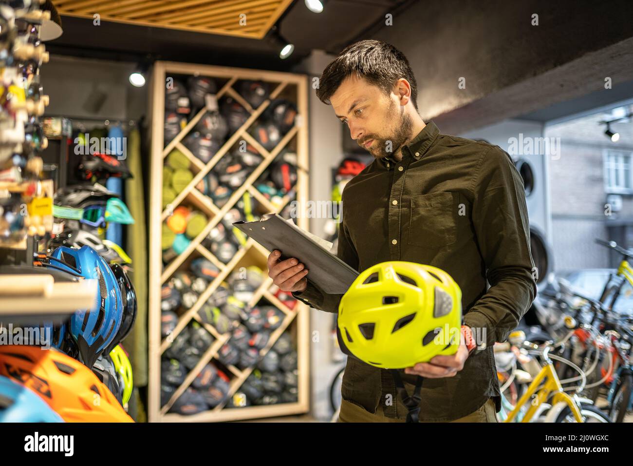 A male bike shop manager makes an inventory of sports helmets in a bike ...