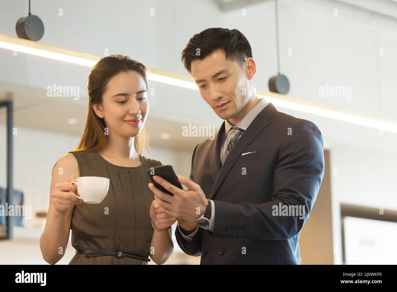 Smiling elegant Chinese business colleagues enjoying coffee and ...