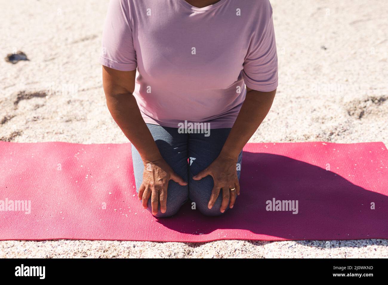 Midsection of senior biracial woman kneeling while practicing yoga on ...
